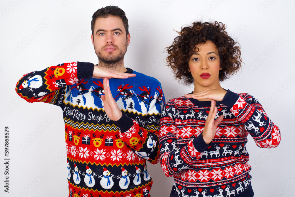 Young couple wearing Christmas sweater standing against white wall ...