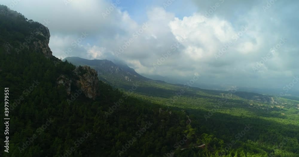 the drone goes up to the clouds through the mountains with green trees ...