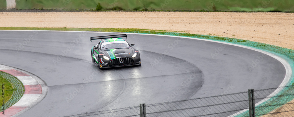 Wet race motorsport Mercedes AMG racing car spraying water at curve on ...