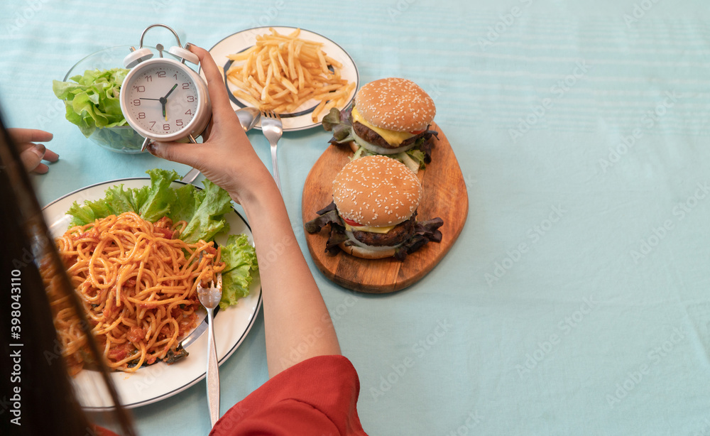 Young woman holding clock and ready to eating a hamburger, French fries ...