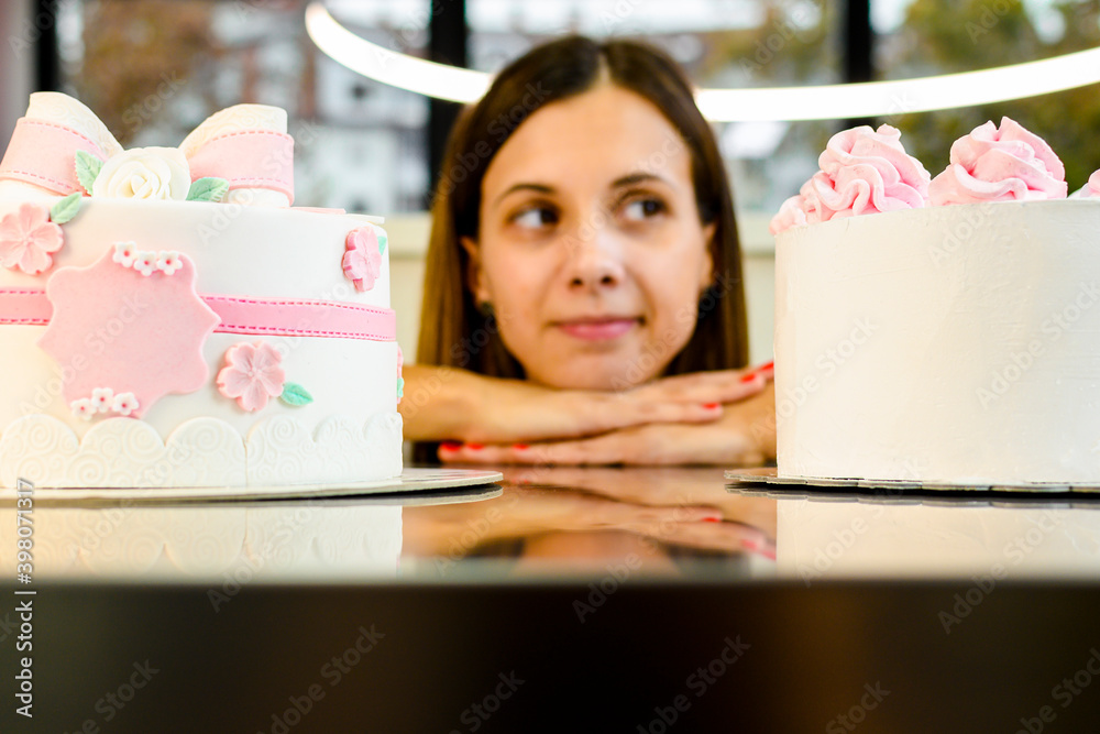 Woman between two cakes. She has smile on her face. She is looking in ...