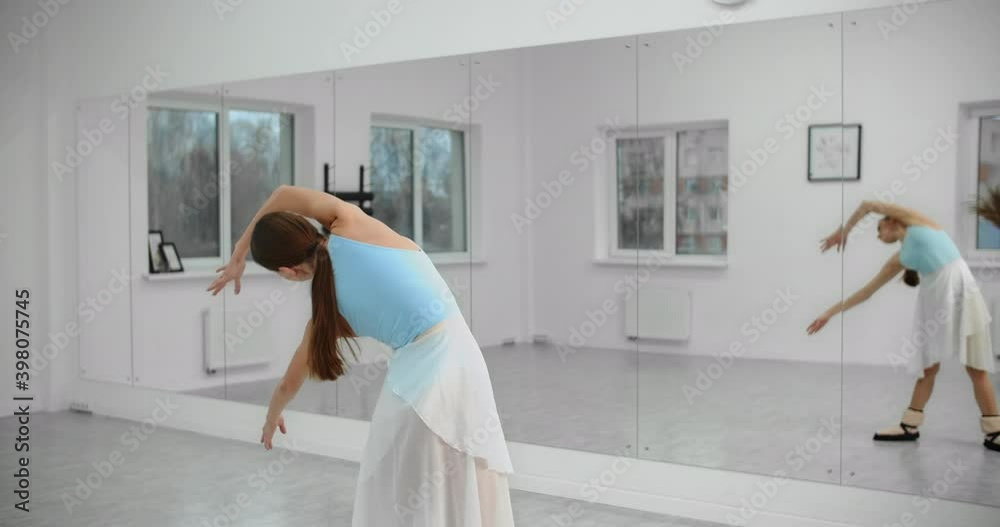 Dancer warms up infront of the mirror wall in the white bright dance hall before rehearsal ...