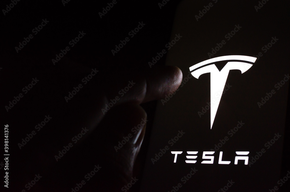 Tesla car logo on a glowing screen and a hand pointing at it. Stock ...