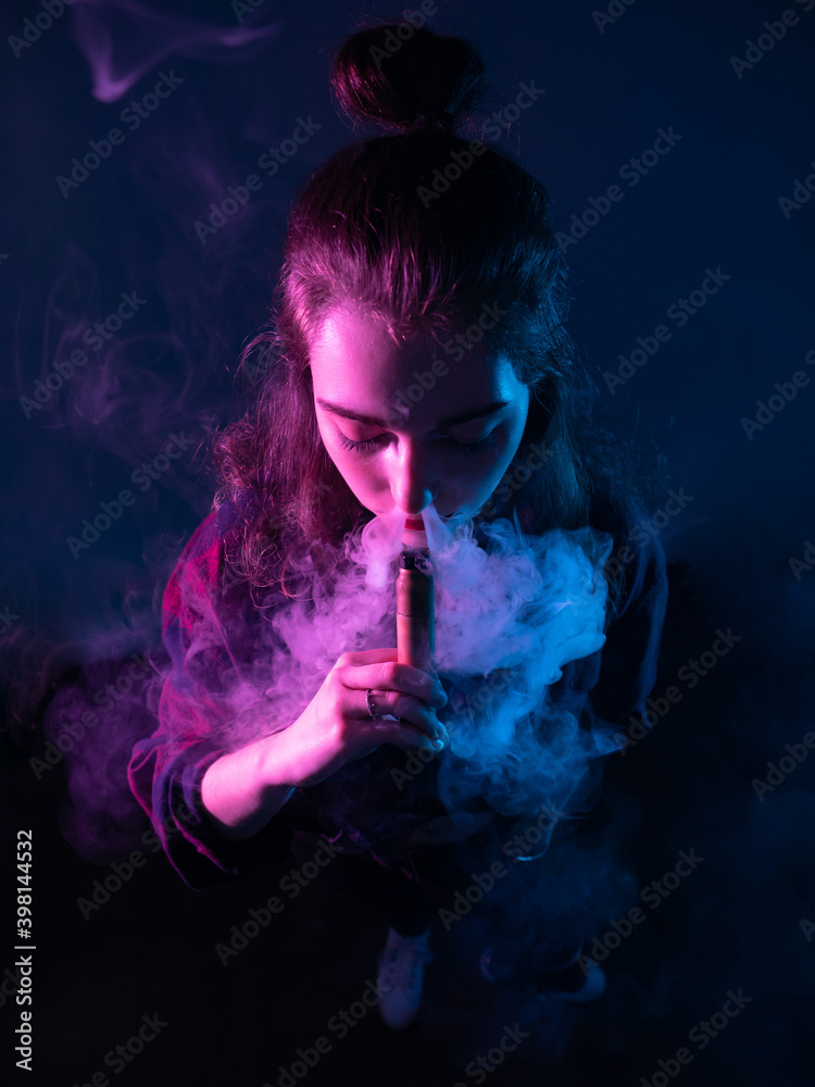 Close-up portrait of woman vaper. She brings vape device to her mouth ...