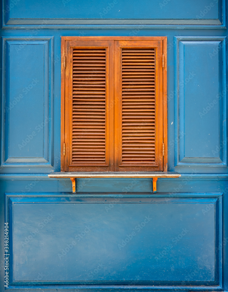 Traditional wooden casement window with slat blinds on blue wall ...