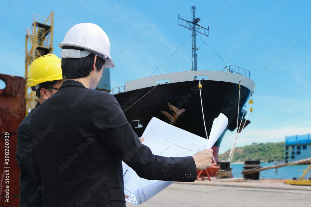 Two engineers reading a blueprint by front cargo ship or shipbuilding ...