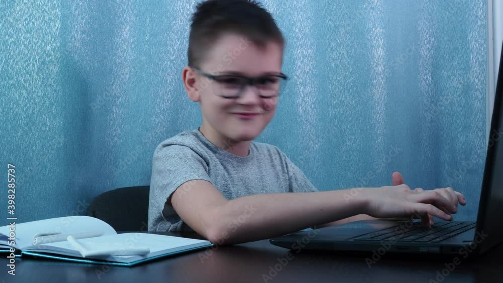 A boy with glasses types on a computer, turns around, laughs and smiles ...