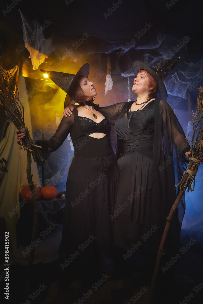 Two adult women looking as witches having fun and posing in dark room ...
