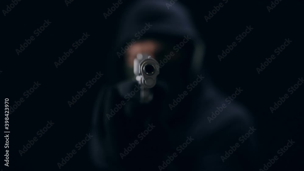 Killer in mask and hood holding real gun over black studio background ...
