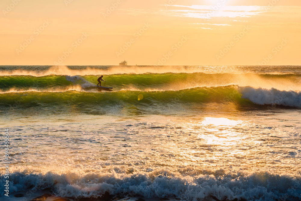 Surfer ride on ocean wave and warm tones of sunset. Surfing in ocean at ...