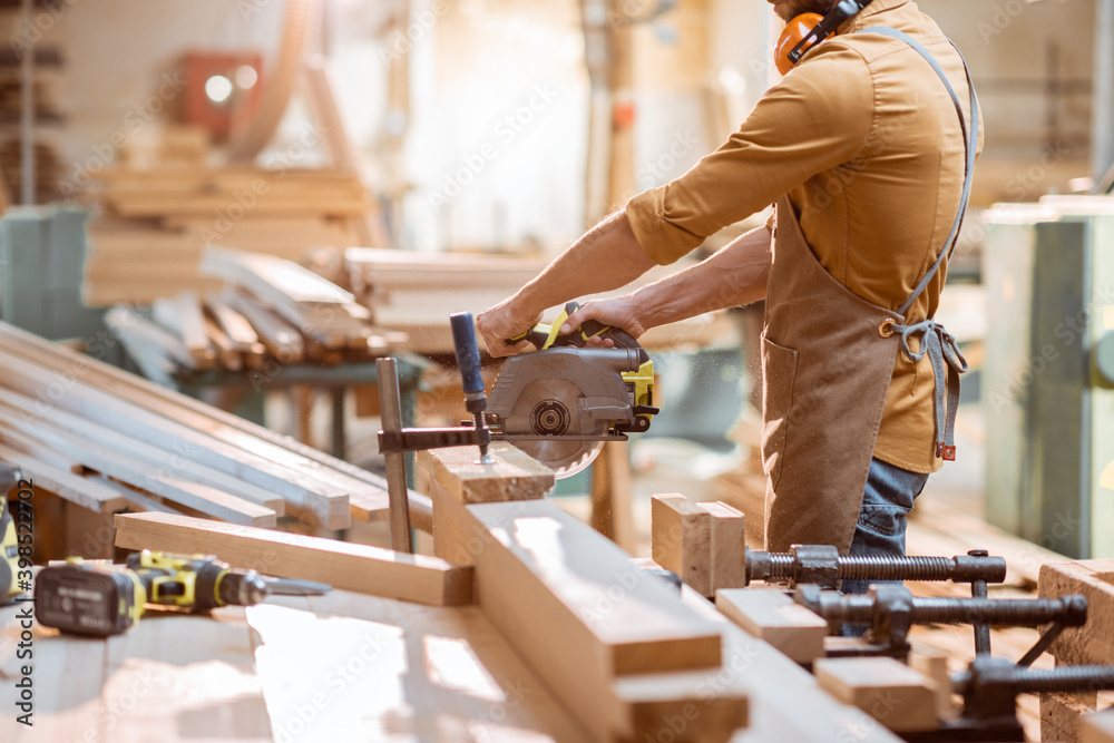 Carpenter sawing wooden bars with cordless electric saw at the joiner's ...