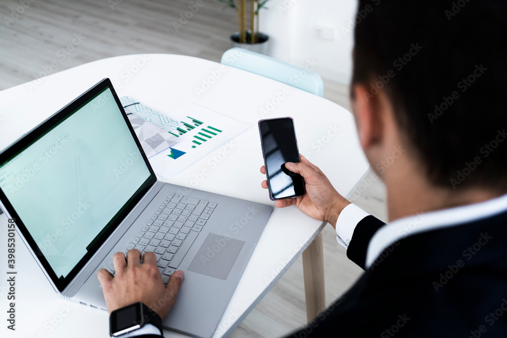 Businessman using mobile phone while sitting with laptop at desk in ...