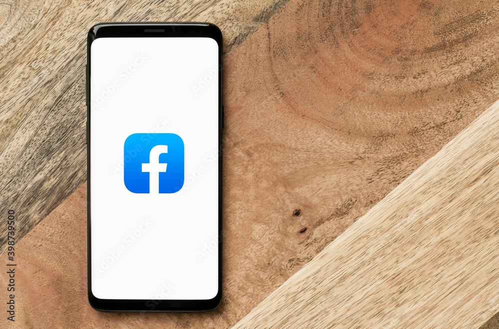Facebook logo app on a smartphone screen, wooden desk background with ...
