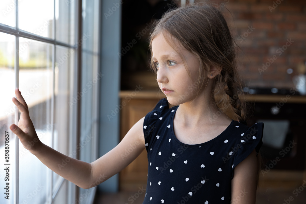 Close up sad upset little girl looking out window, touching glass ...