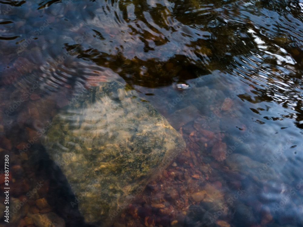 Colorful gravel on bottom of rapid shallow stream visible through clear ...
