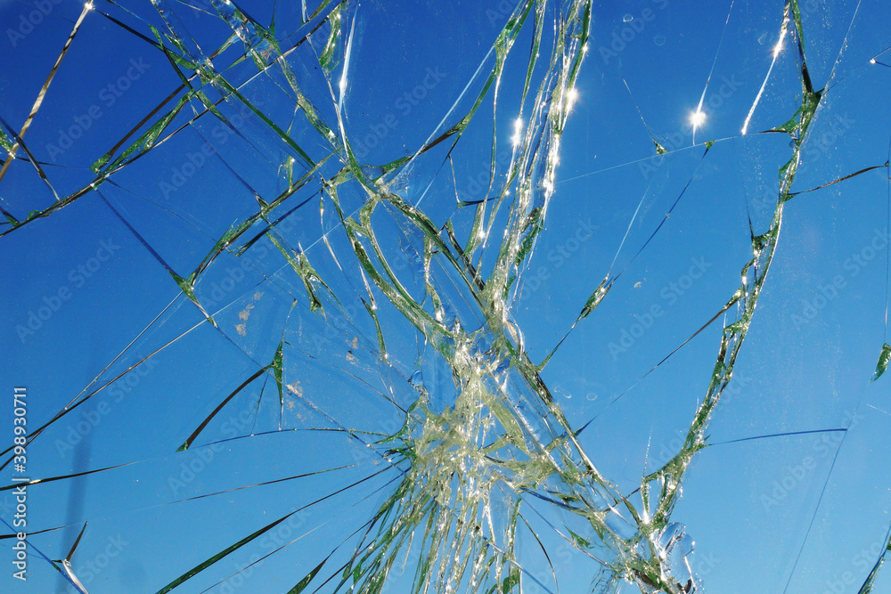 Broken glass with cracks and sun glare on the background of the blue ...