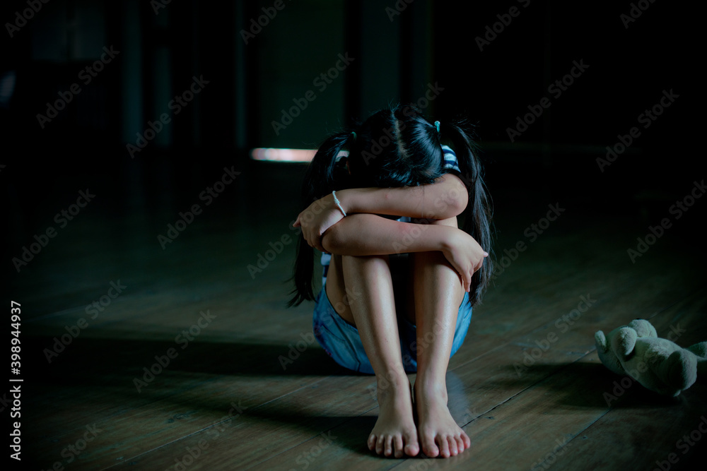 Serious little child girl sitting alone in dark room.Low key style ...