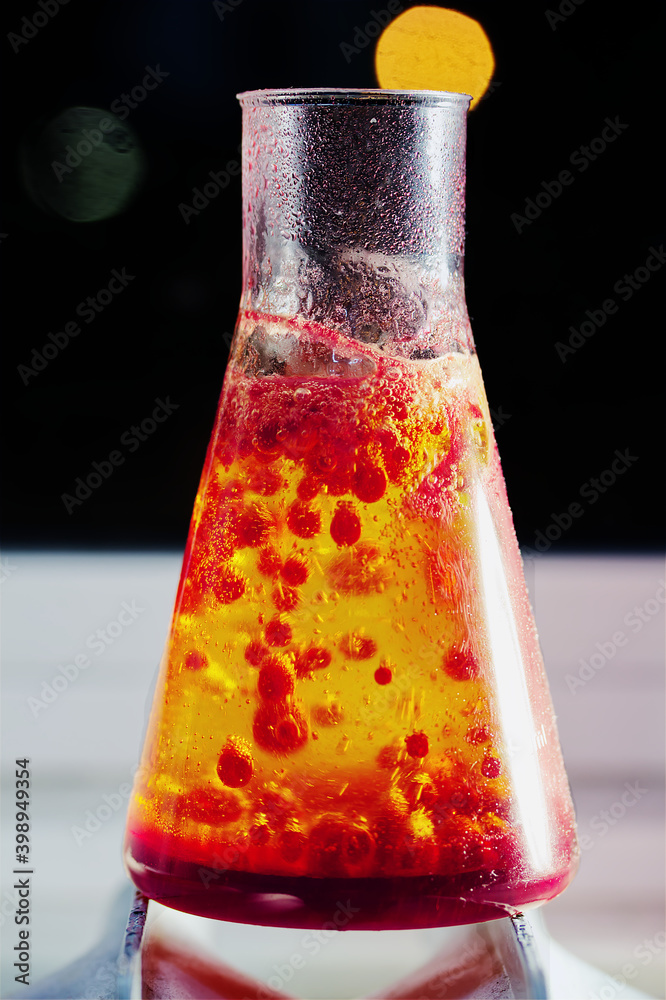 Matraz sobre superficie blanca. En un líquido dorado se mueven gotas de ...