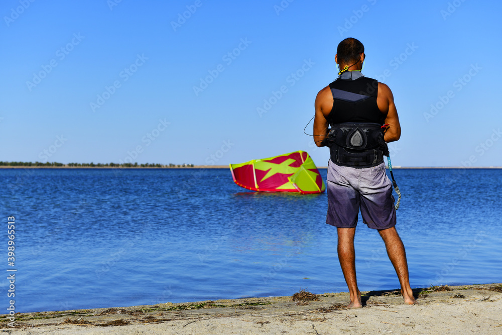 A male kitesurfer stands on the shore of the bay, waiting for the wind ...