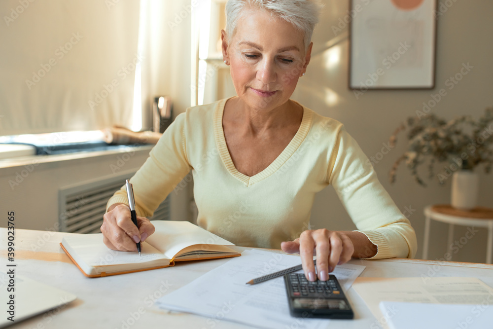 Concentrated middle aged woman with short hair calculating income and ...