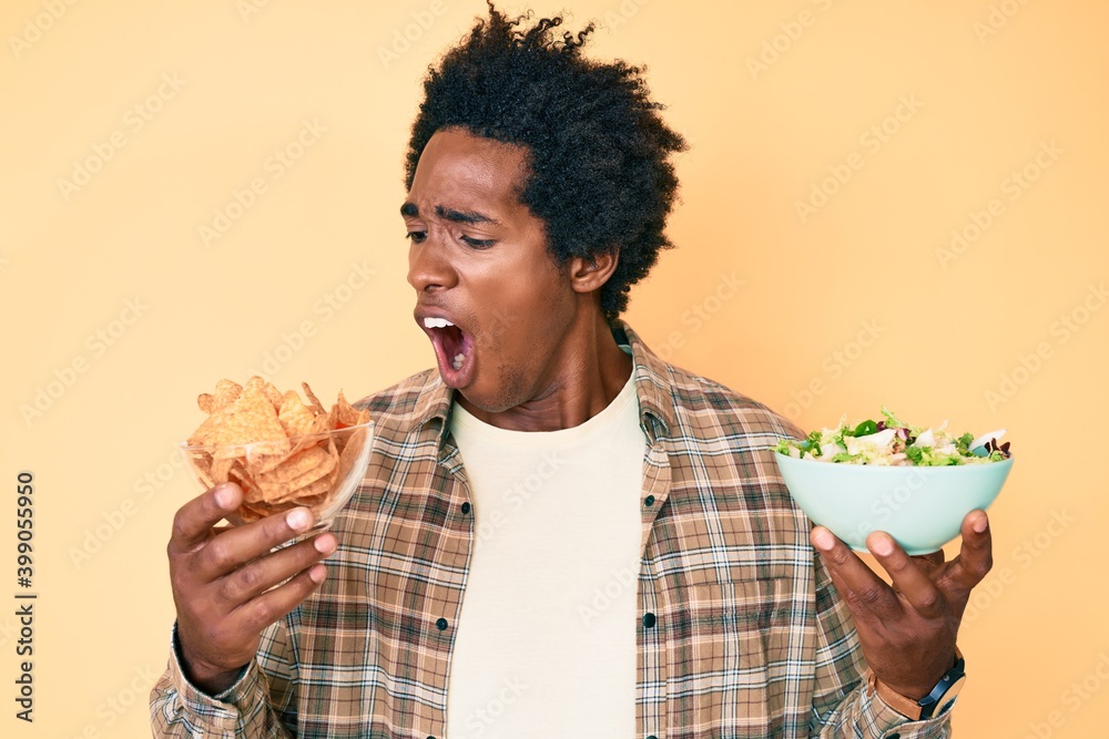 Handsome african american man with afro hair holding nachos and healthy ...