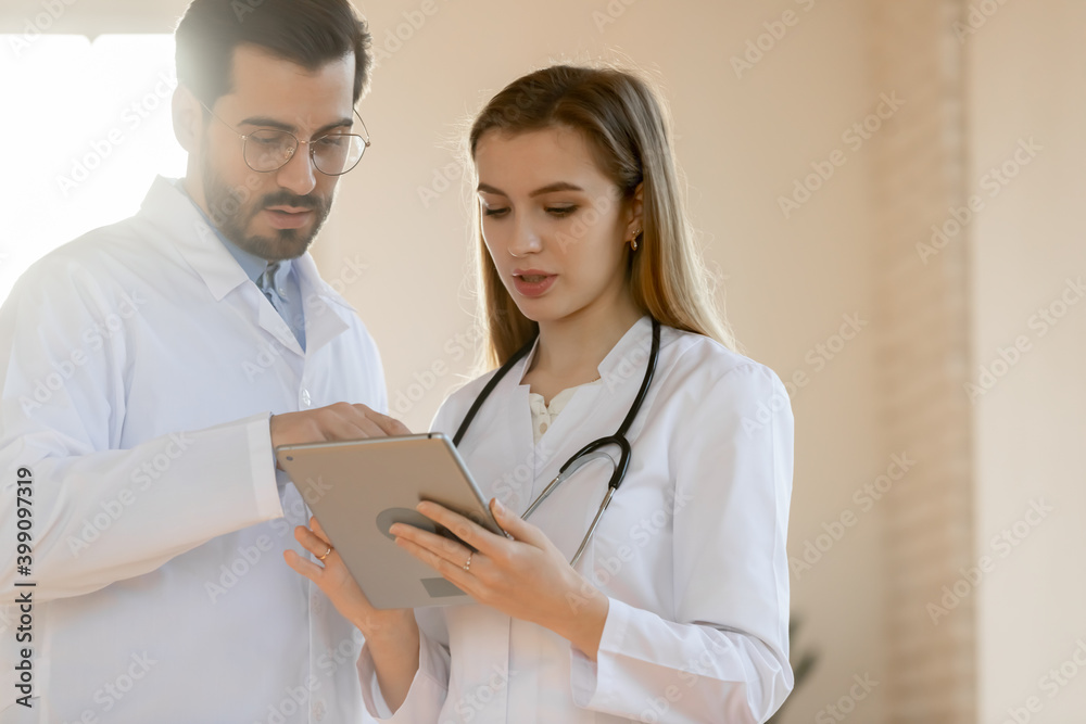 Two diverse doctors in white medical uniforms look at tablet screen ...