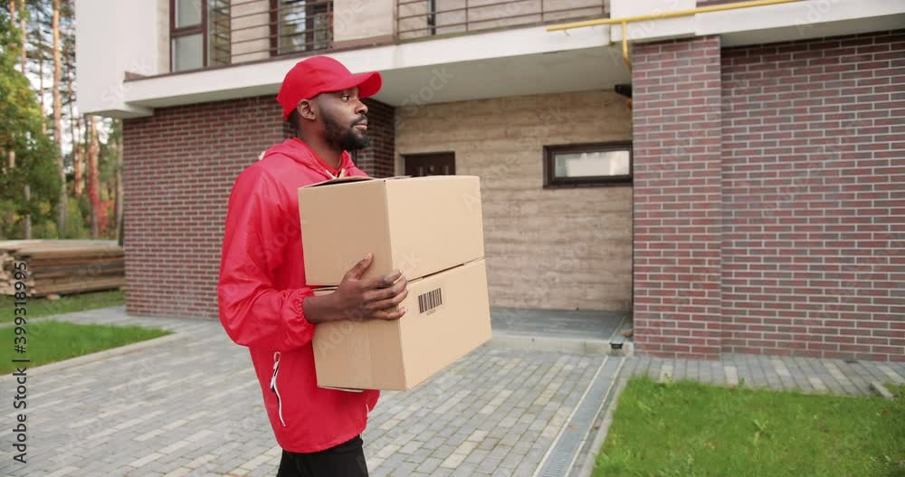 Portrait of young male courier in red jacket with big boxes walking on ...
