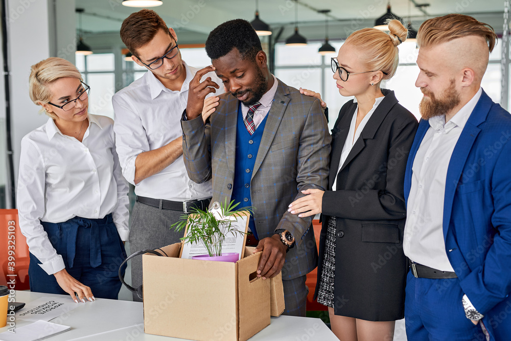 sad black male is supported by colleagues, he is fired from work due to ...