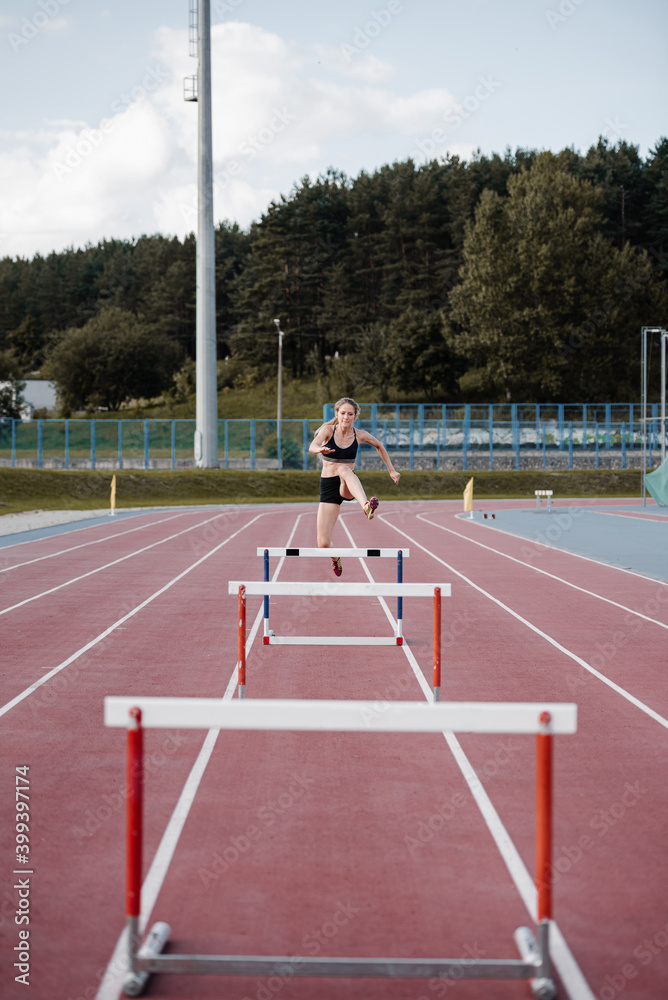 Female athlete leaping over barrier at stadium Stock Photo | Adobe Stock