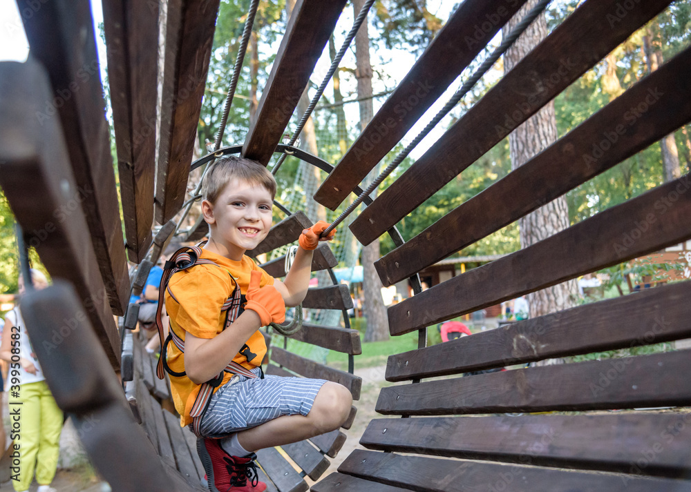 Happy kid overcomes obstacles in rope adventure park. Summer holidays ...