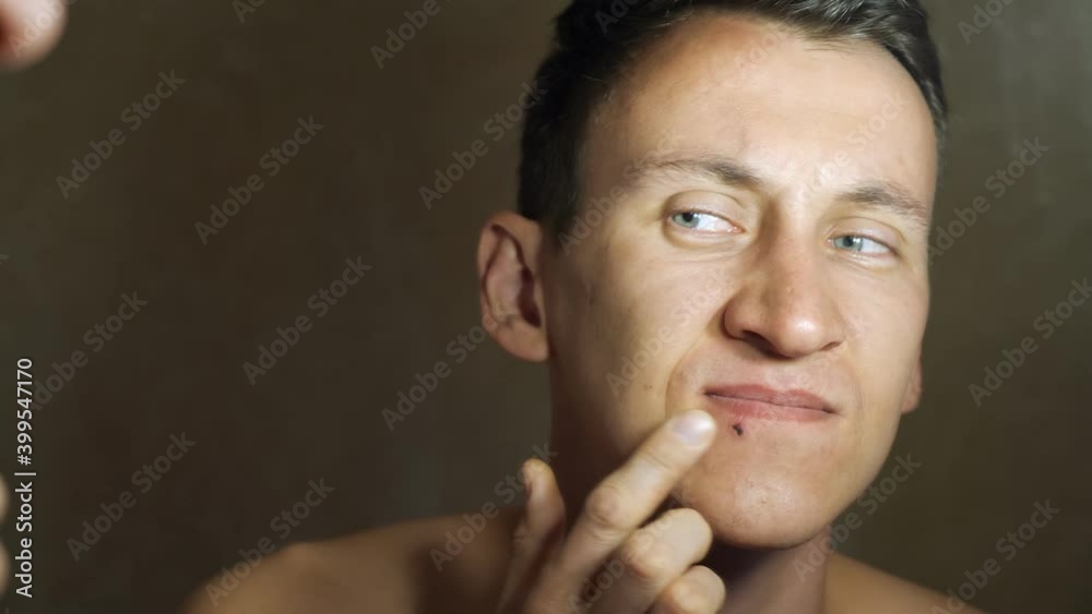 Man with grey eyes looks carefully at mirror reflection of face and ...