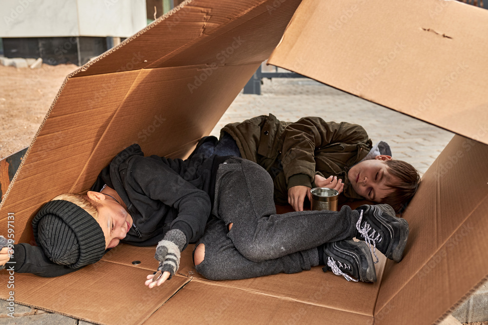 Foto de two abandoned children lie under cardboard begging, homeless ...