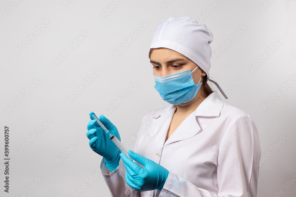 A nurse in a robe and a medical cap and gloves holds a syringe ...