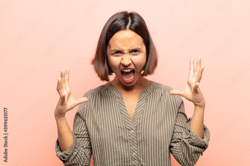 young hispanic woman screaming in panic or anger, shocked, terrified or ...