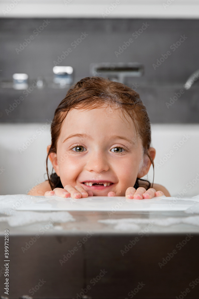 Foto de Cute young girl with toothless smile peeking over bathtub do ...