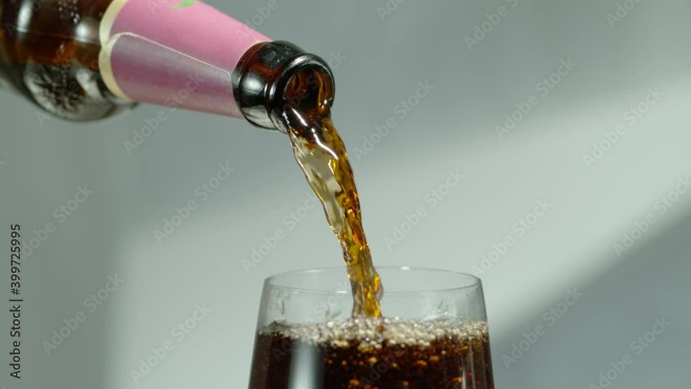 Pouring a fizzy drink from a bottle in a glass in slow motion on gray ...