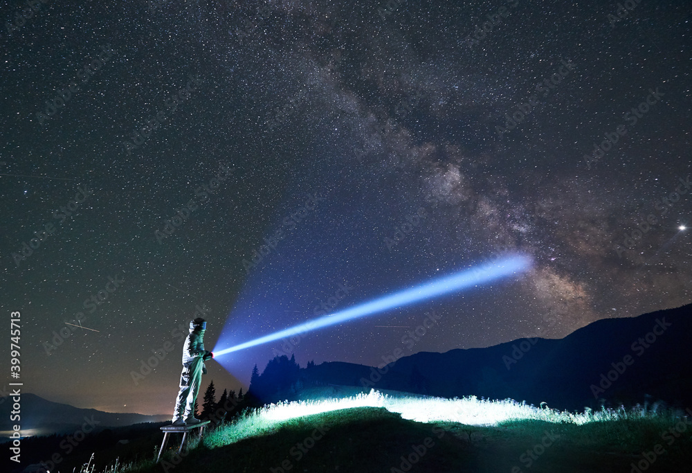 Spaceman astronaut illuminating beautiful starry sky with flashlight at ...