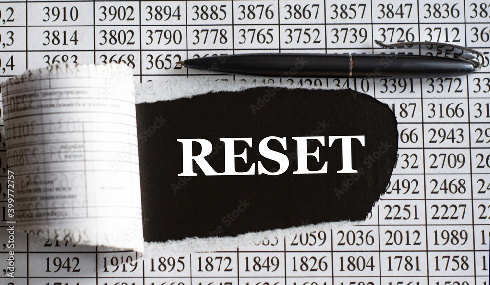 RESET is the word behind torn office paper with numbers and a black pen ...