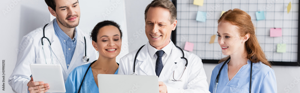 Smiling multiethnic doctors with nurses using devices in hospital ...