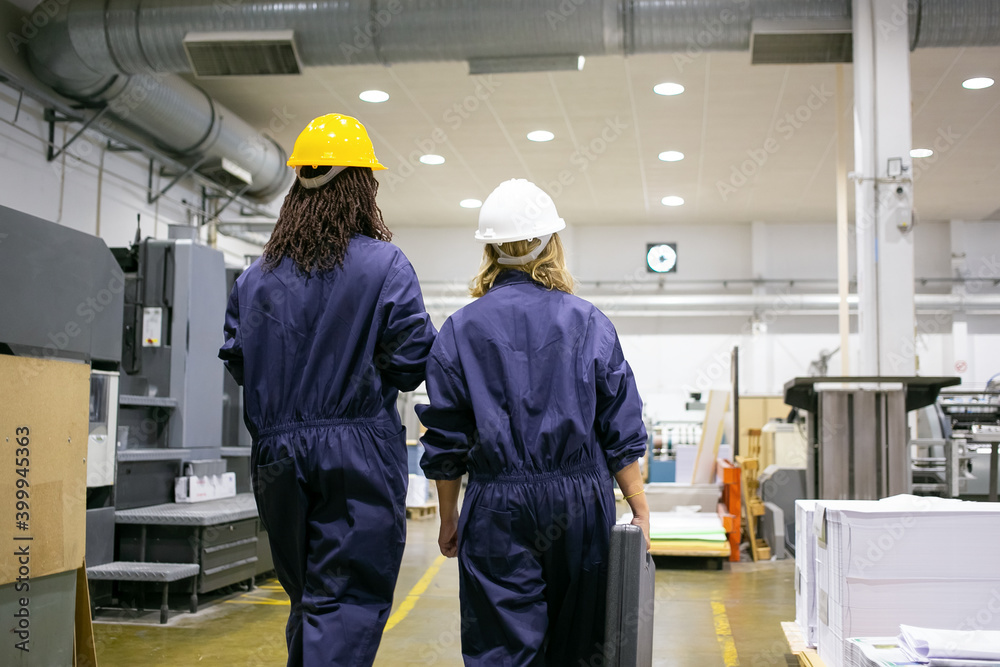 Diverse female factory workers in hardhats and overalls walking on ...