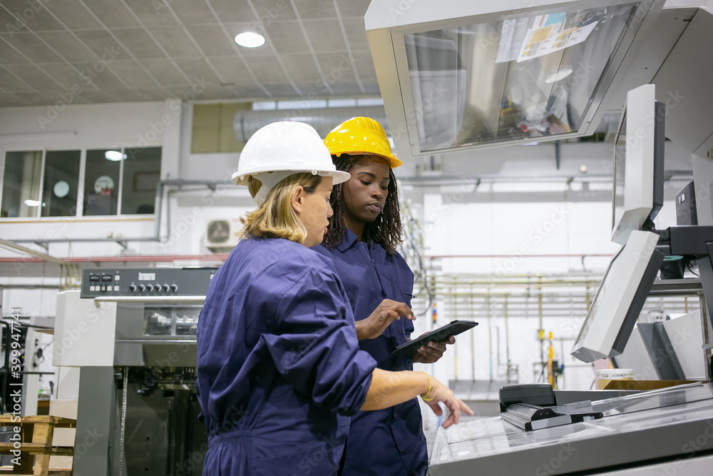 Female industrial employee teaching colleague to operate machine ...