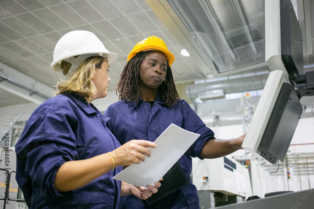 Black female industrial employee teaching colleague to operate machine ...