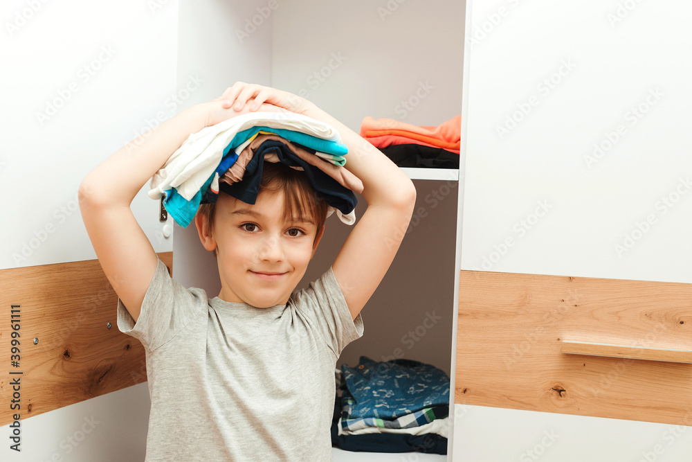 Happy boy holding stack of clothes on his head. Kid organizing clothes ...