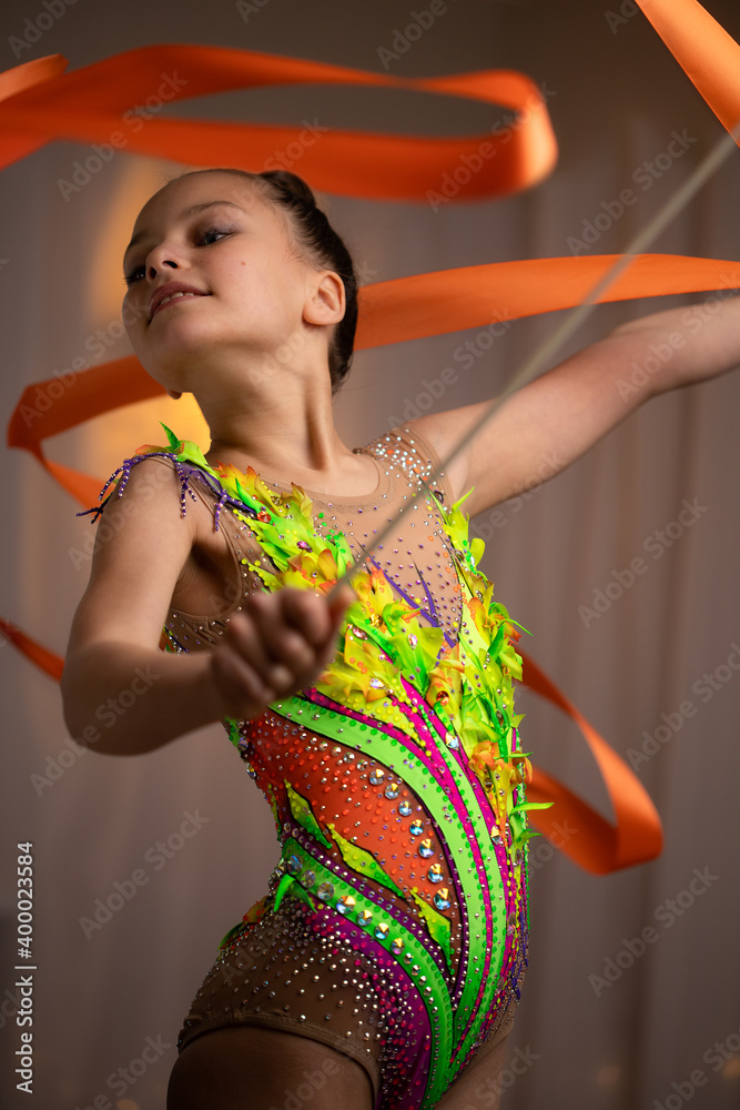 Preteen girl gymnast in colorful bright leotard dancing with orange ...
