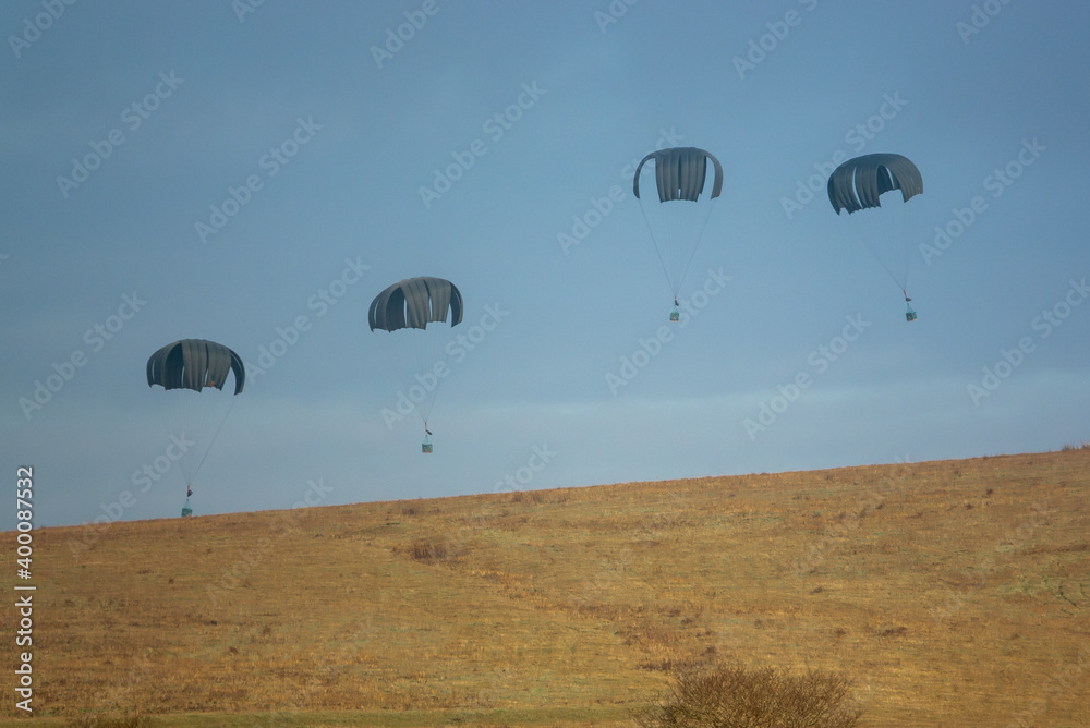 four large cargo drop parachutes about to hit the ground, dropped from ...