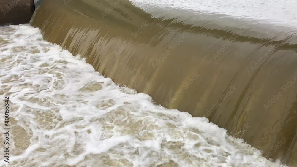 River flows over a dam. Stormy brown dirty muddy brown water filters ...