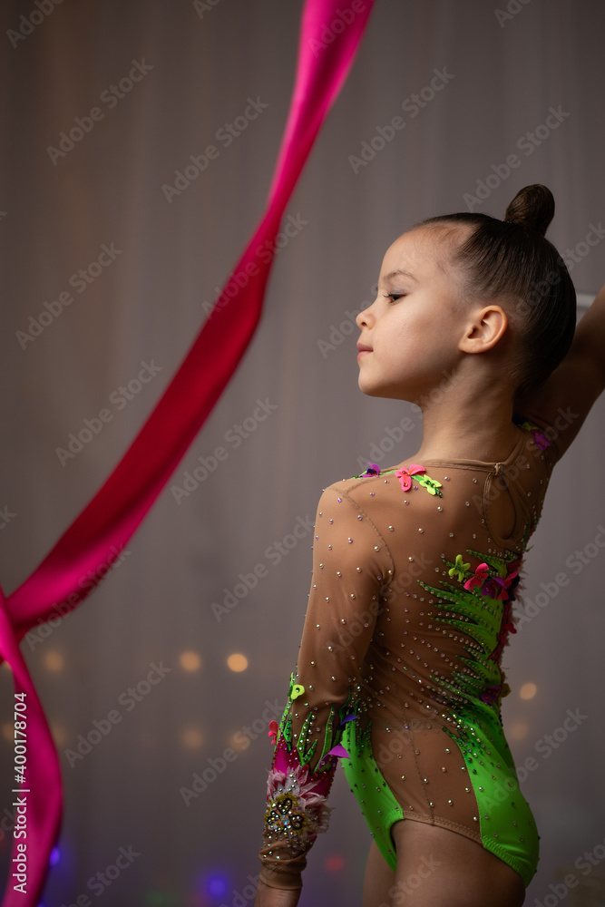 Little girl gymnast in colorful bright leotard dancing with crimson ...
