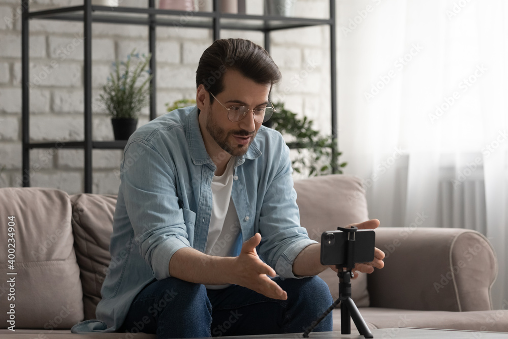 Hand free. Millennial male sitting on sofa before webcam of smartphone ...