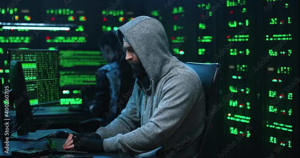 Male hacker with beard in hood hacked into database in office while ...