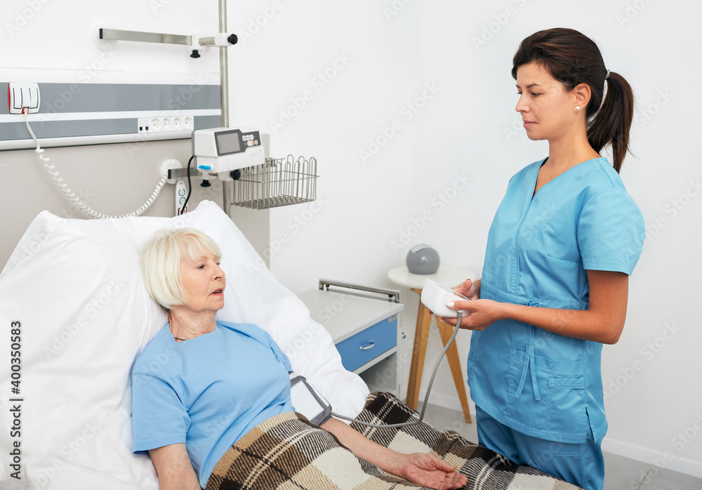 Geriatric nurse measures the pressure of a senior woman patient who is ...